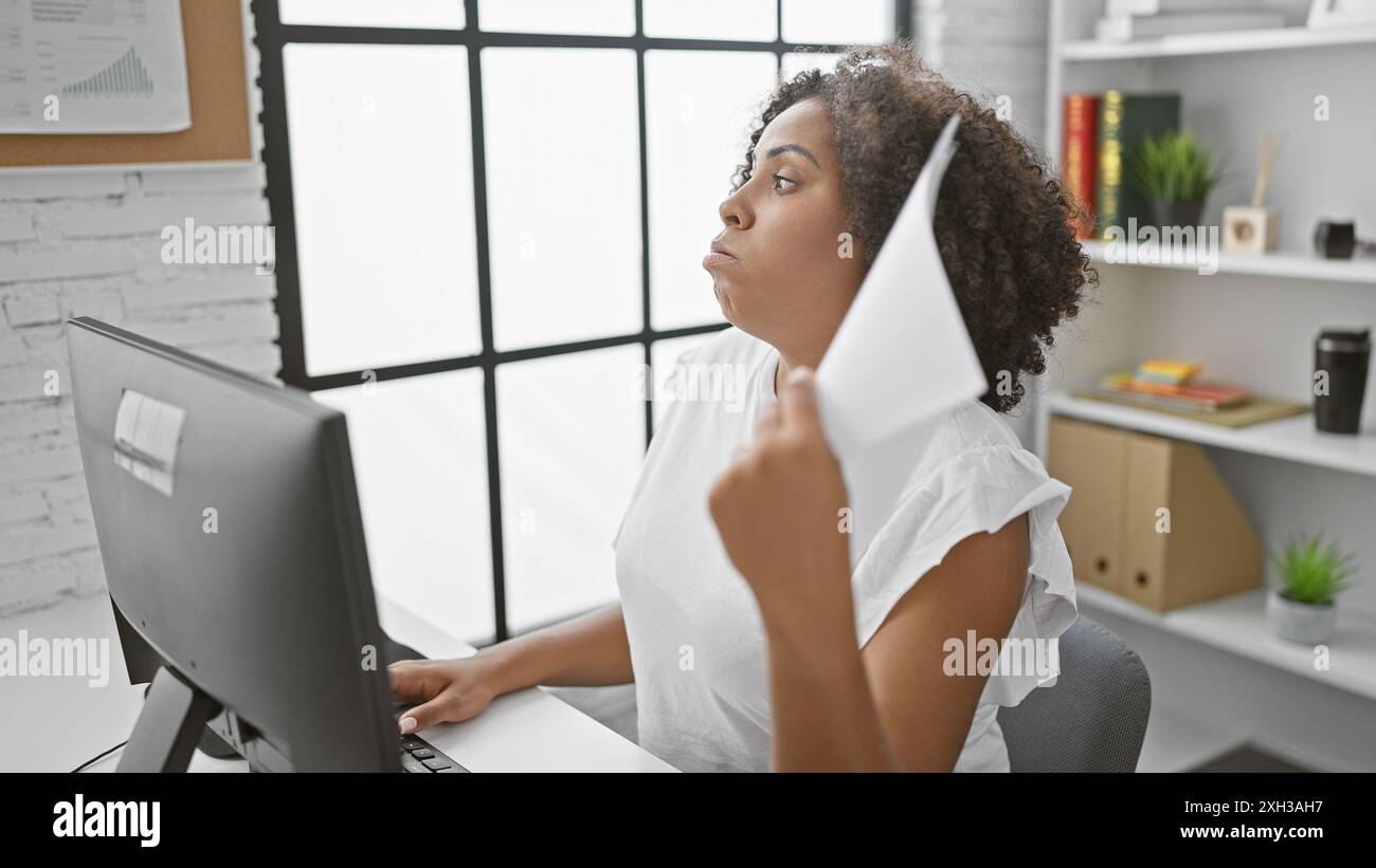 African american woman fanning herself with paper in a modern office ...