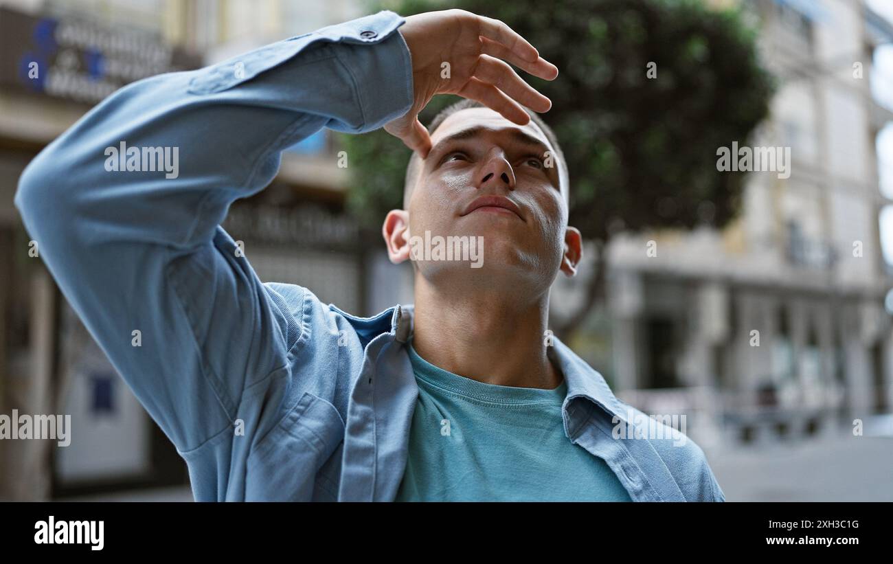 A young hispanic man in casual attire shields his eyes from the sun on ...