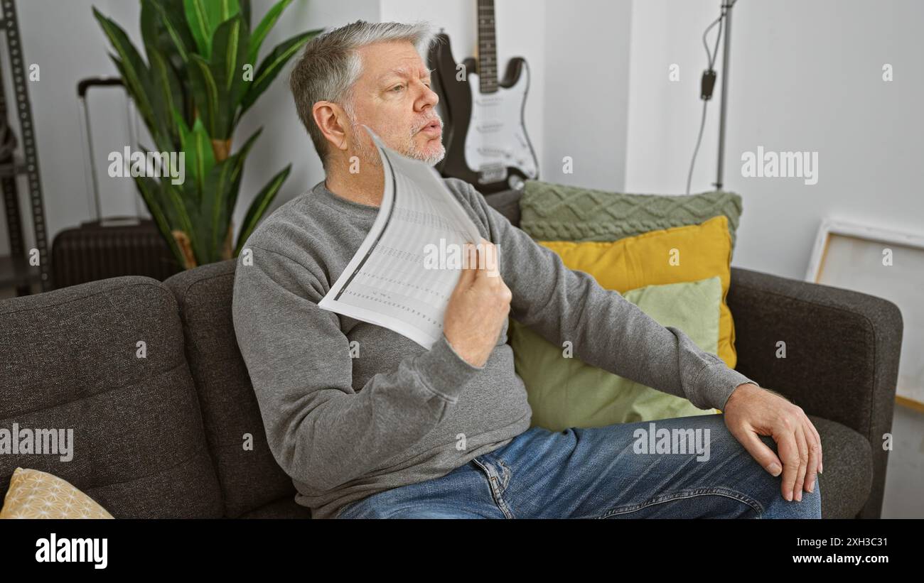 Mature man fanning himself with paper sitting on a couch indoors ...