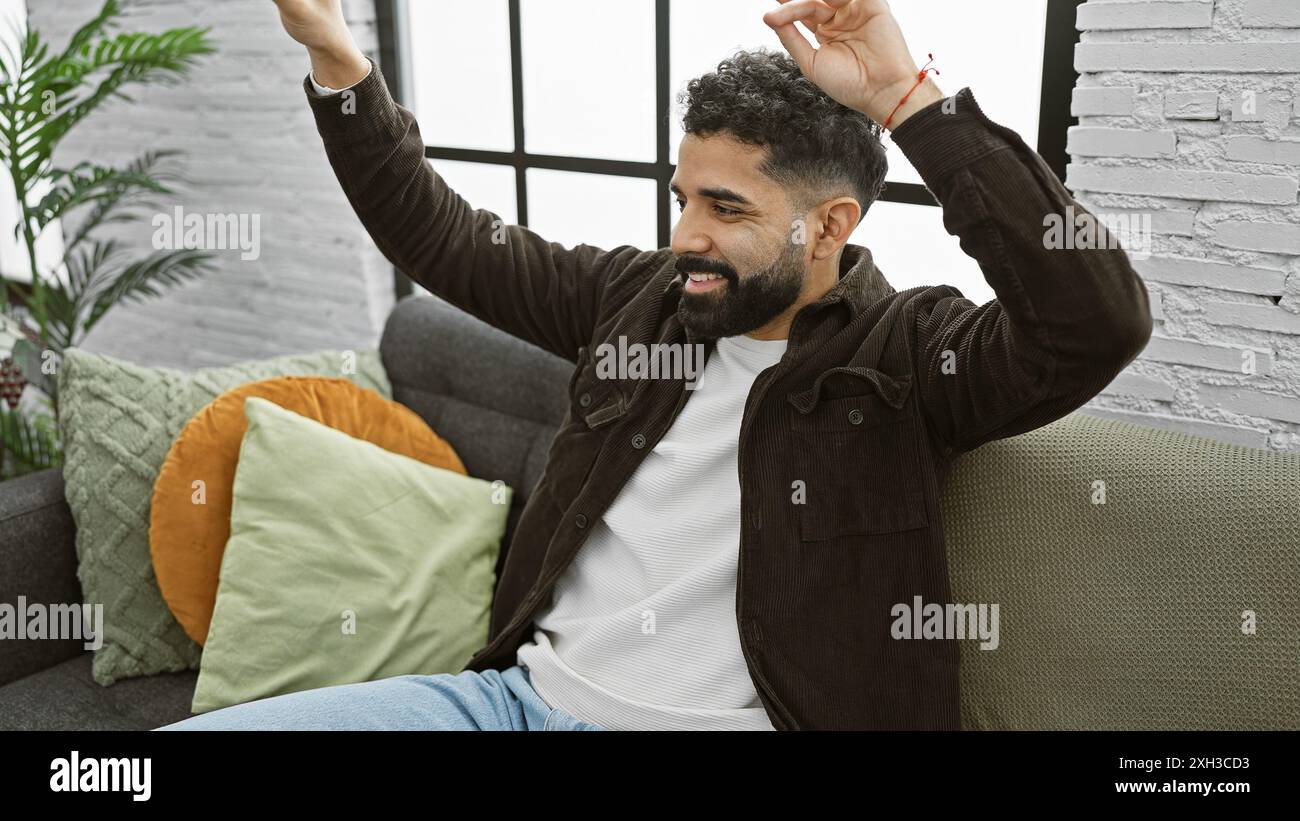 A handsome young hispanic man with a beard relaxes on a couch in a well ...