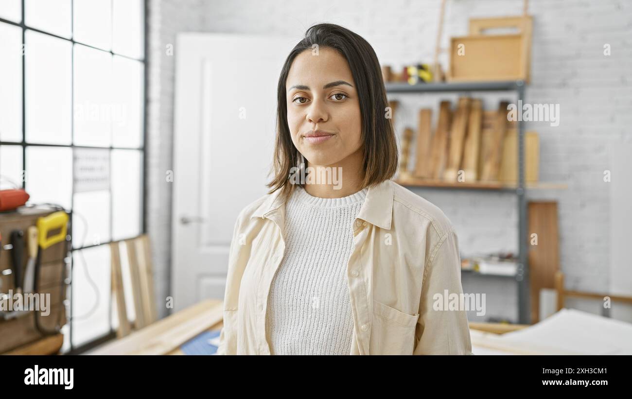 A confident young woman stands in a well-lit carpentry workshop, exuding professionalism and ...