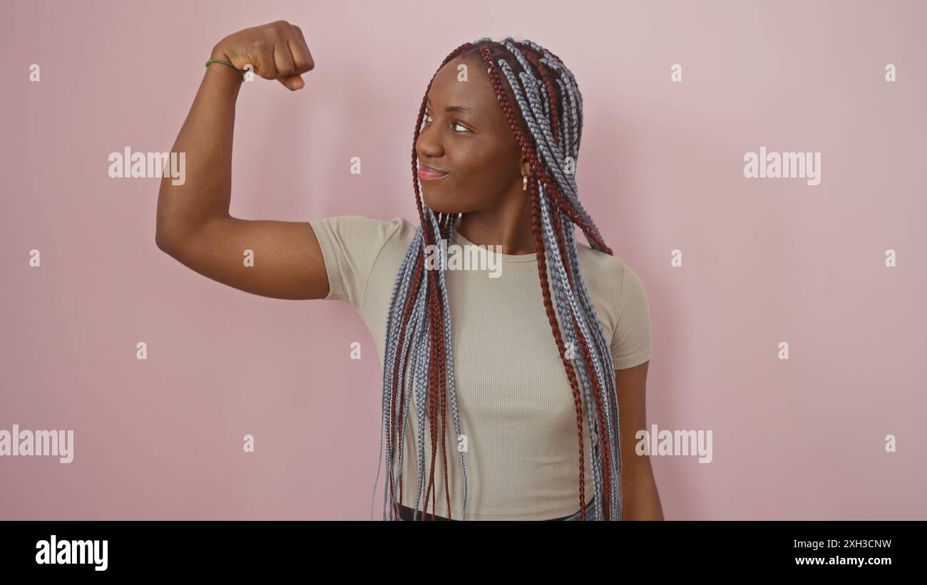 Confident african woman with braids flexing her muscle against a pink ...