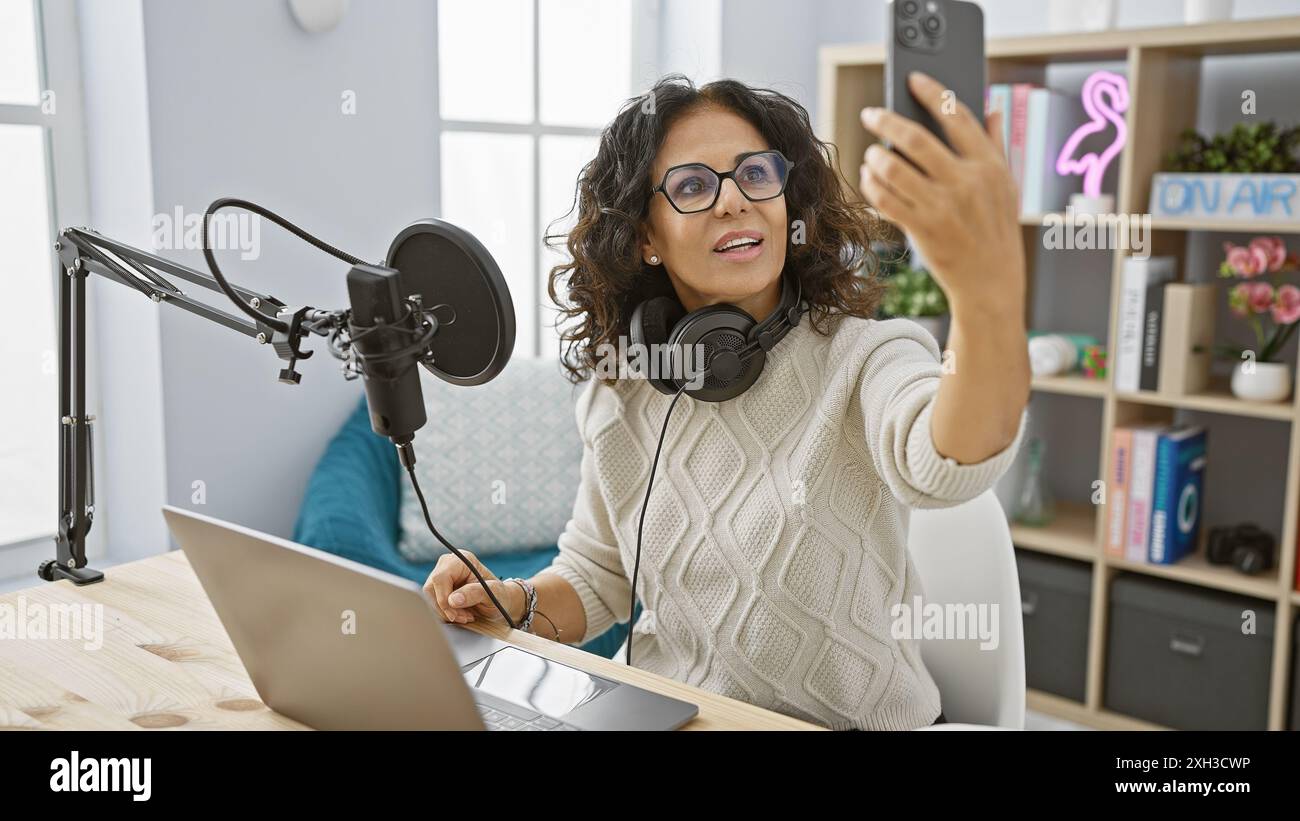 A middle-aged hispanic woman takes a selfie in a modern radio studio ...