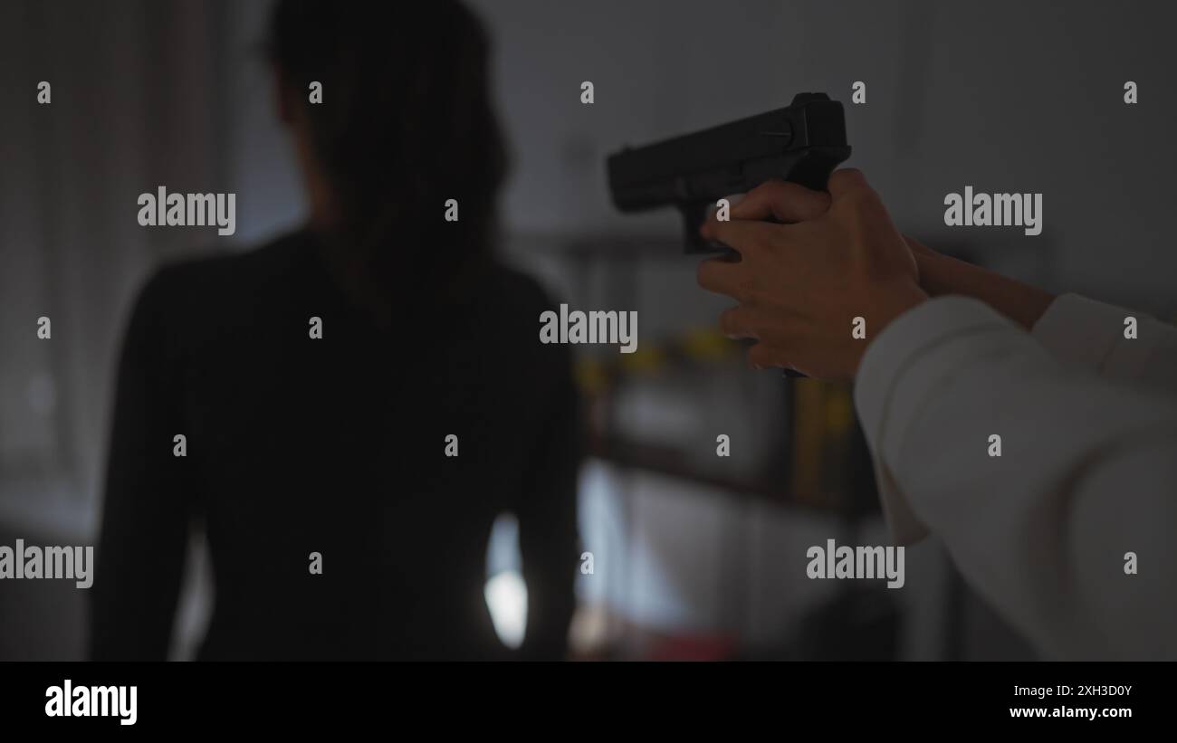 An armed person points a handgun at a woman's back in a dimly lit ...