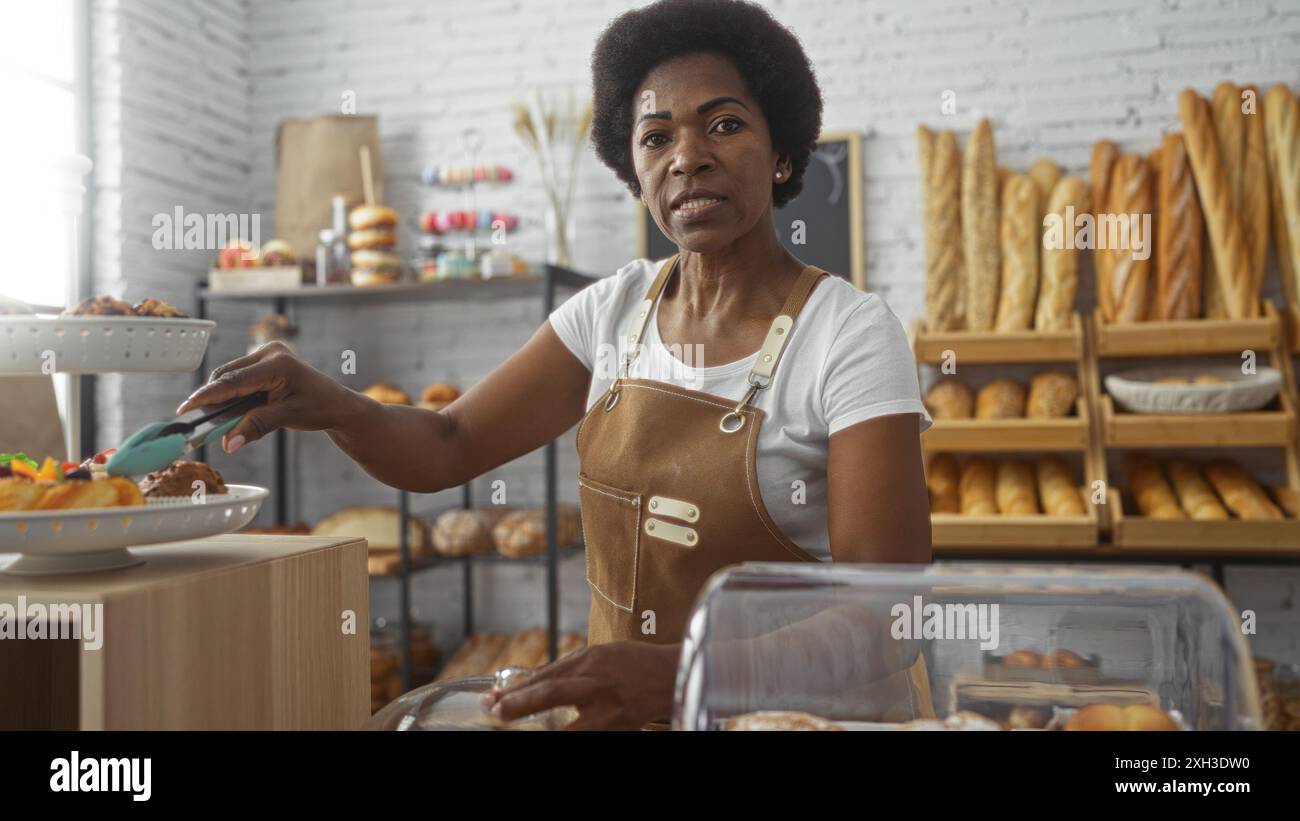 African american woman with curly hair arranging pastries in a bakery ...