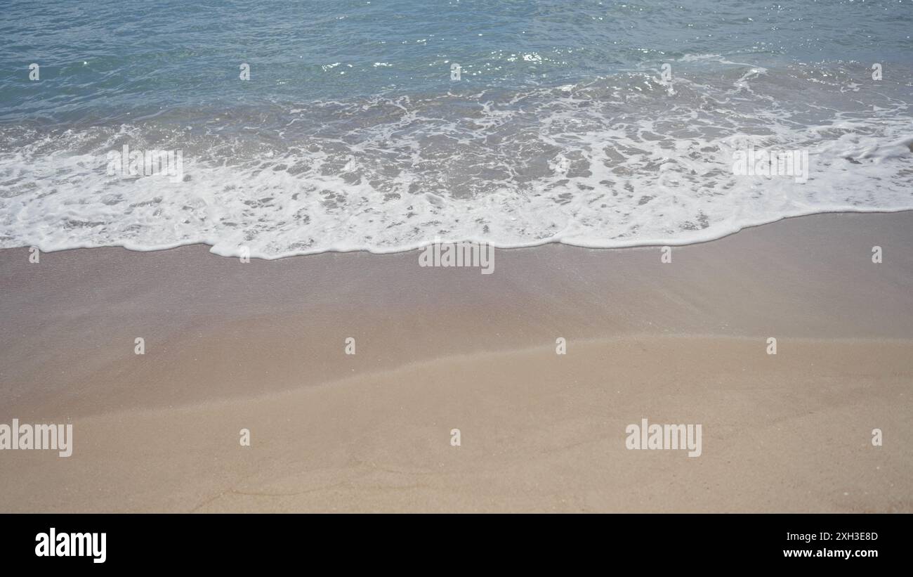 Sandy shore meets foamy ocean waves under clear blue skies Stock Photo ...