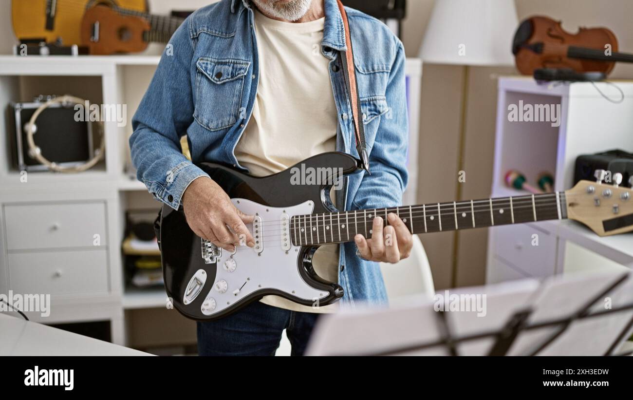 A mature man in casual attire plays an electric guitar in a modern room ...