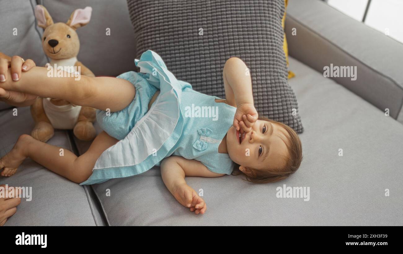 Toddler girl lying on a couch in a living room playing with a toy ...