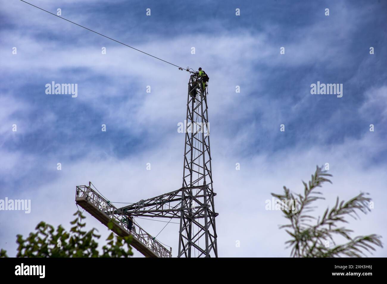 Worker in high visibility clothing atop a electricity pylon tower ...