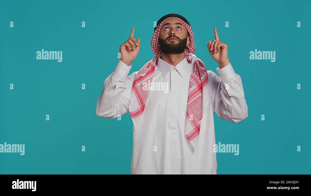 Middle eastern man pointing above head, looking up and indicating ...