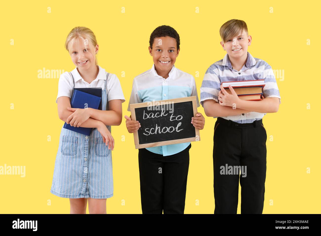 Little classmates in stylish uniform holding blackboard with text BACK ...