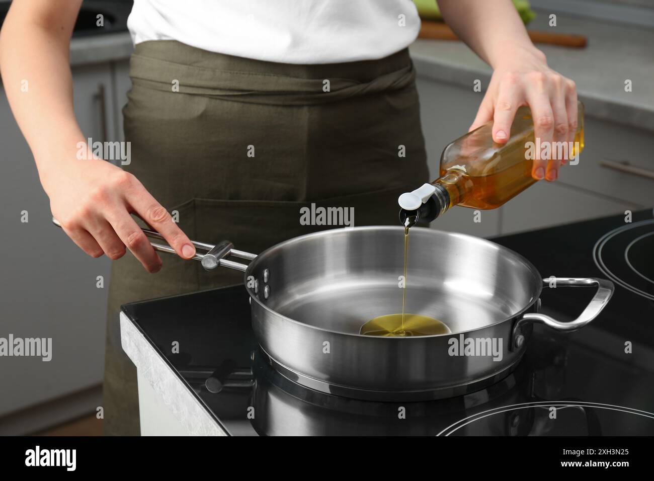 Vegetable fats. Woman pouring oil into frying pan on cooktop in kitchen ...