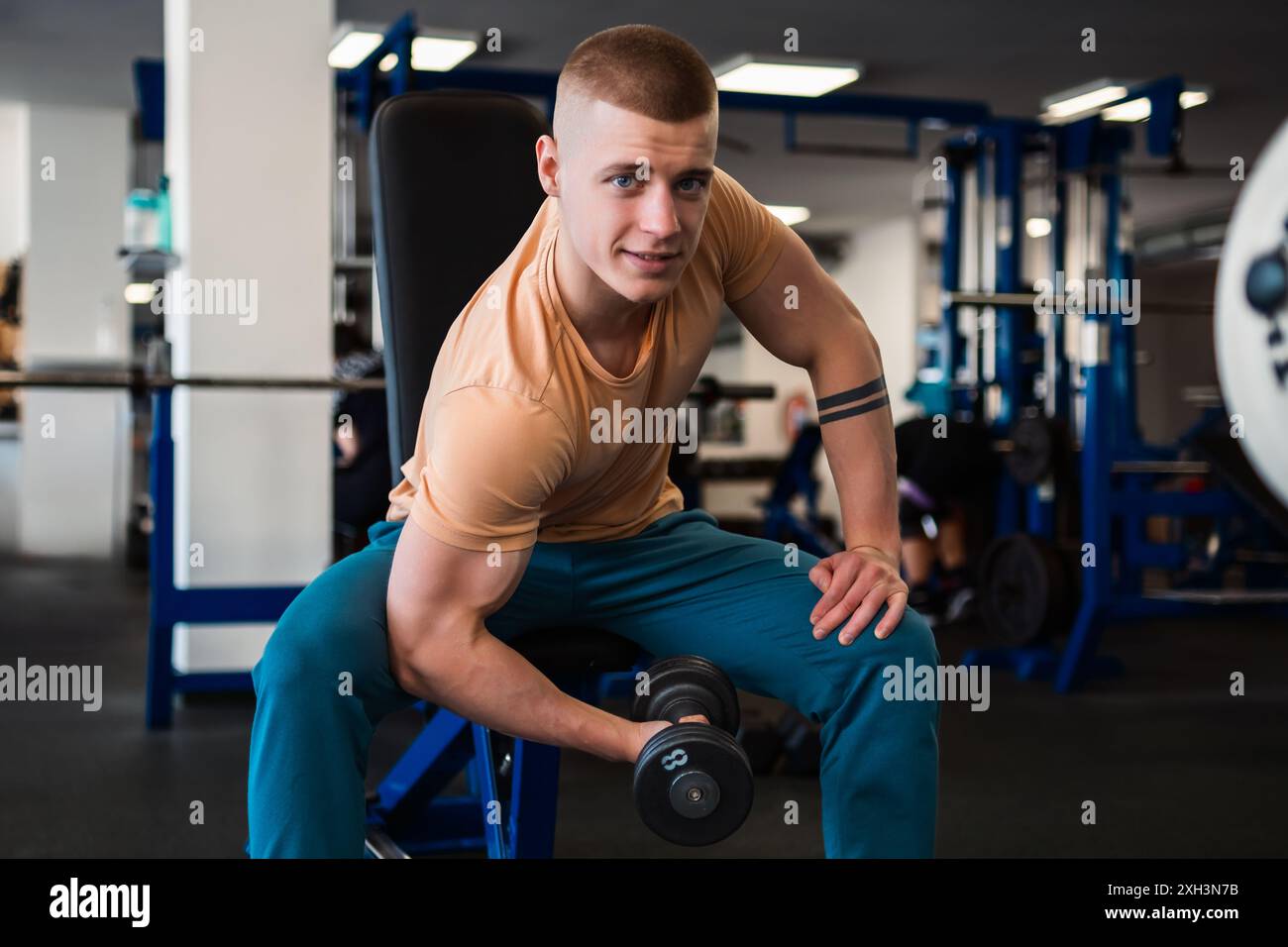 Bodybuilder performs bicep curls with a dumbbell while sitting on a ...