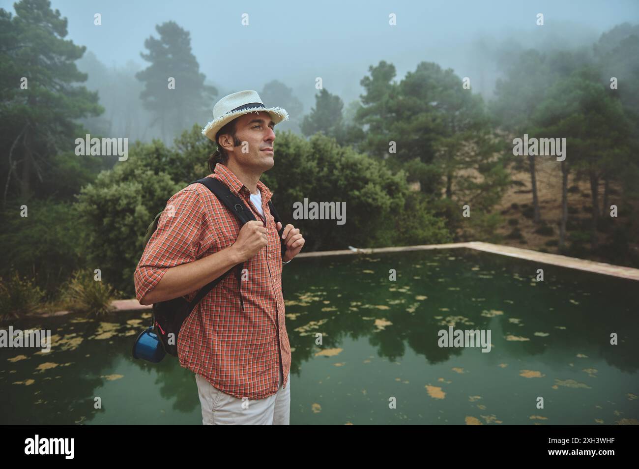 A hiker stands beside a forest pond, soaking in the tranquil atmosphere ...