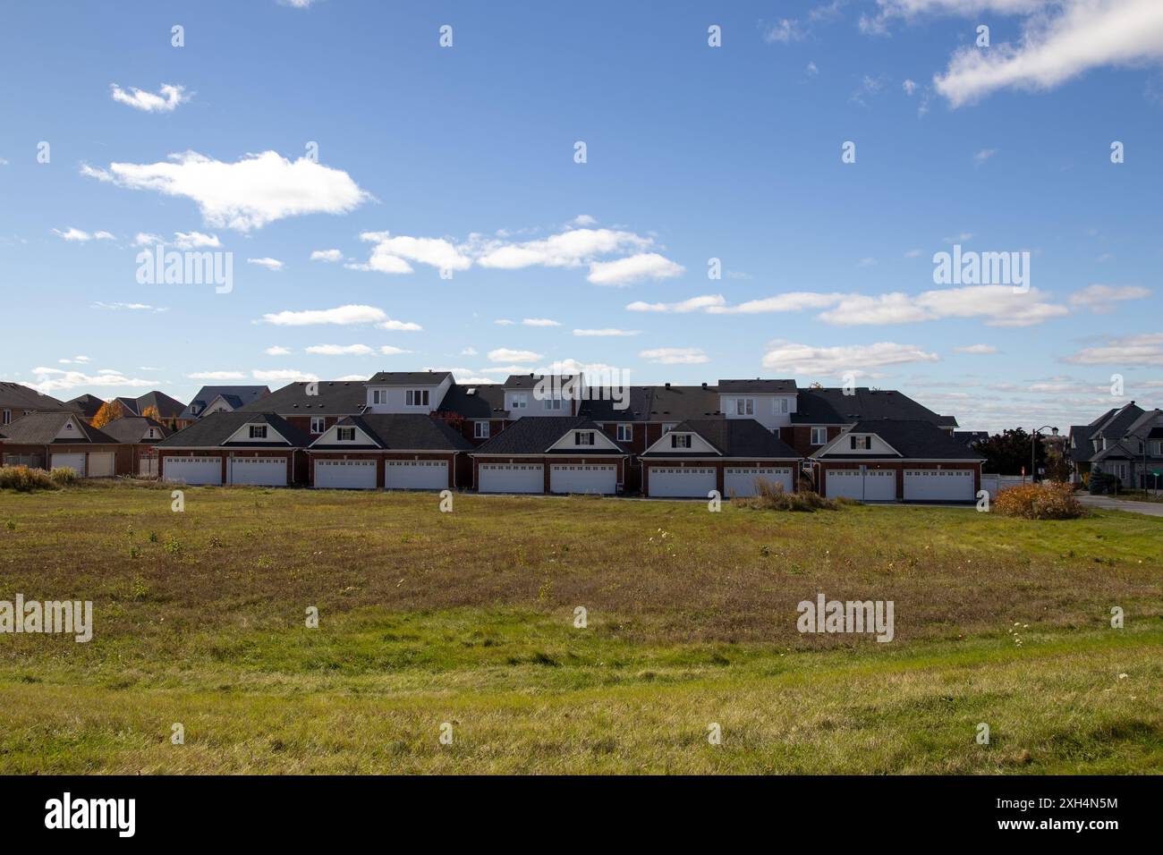 Row of identical suburban houses with white garages and green lawns ...
