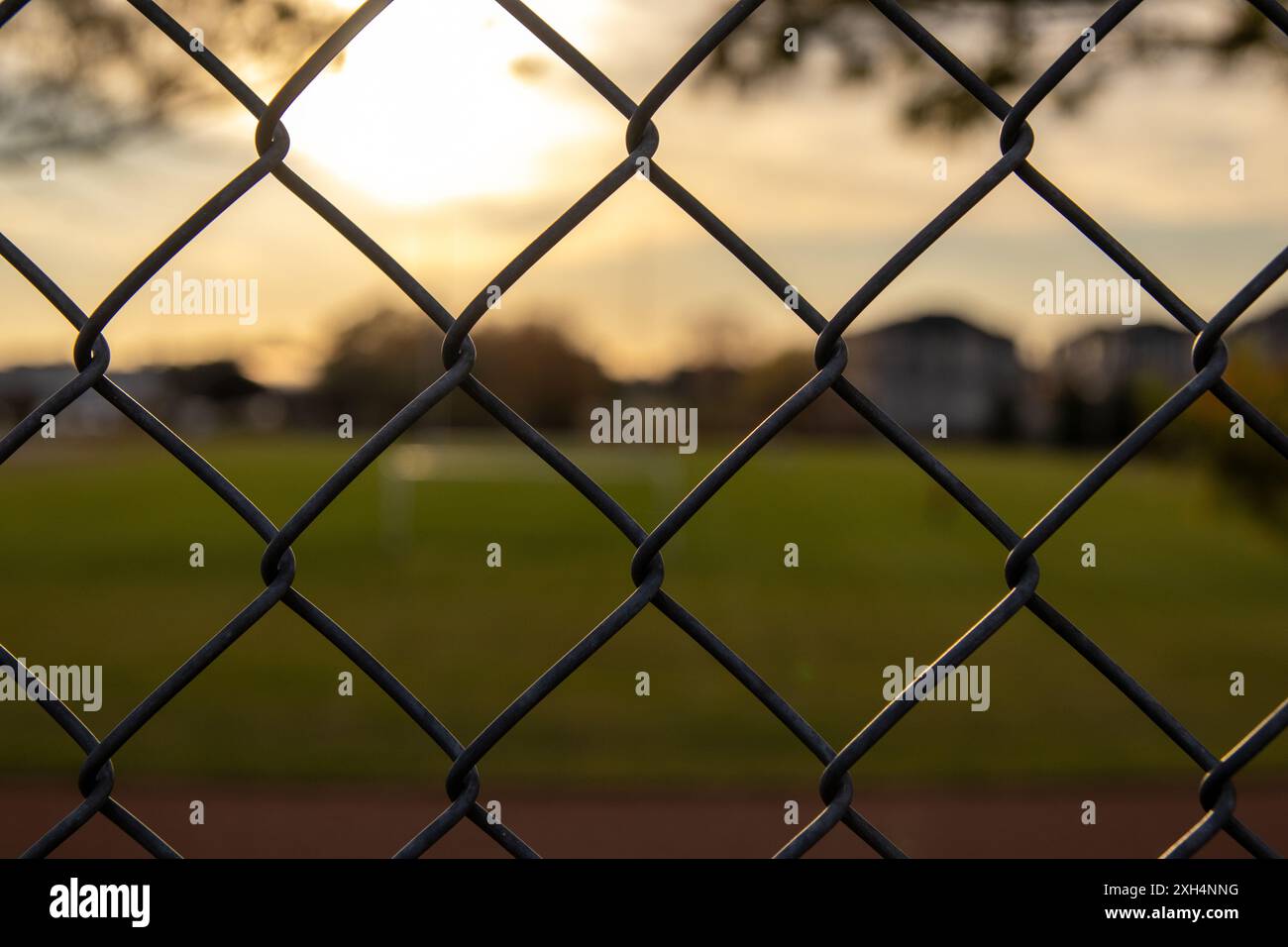 Sunset-lit chain-link fence foreground - blurred sports field background - warm golden hour ...