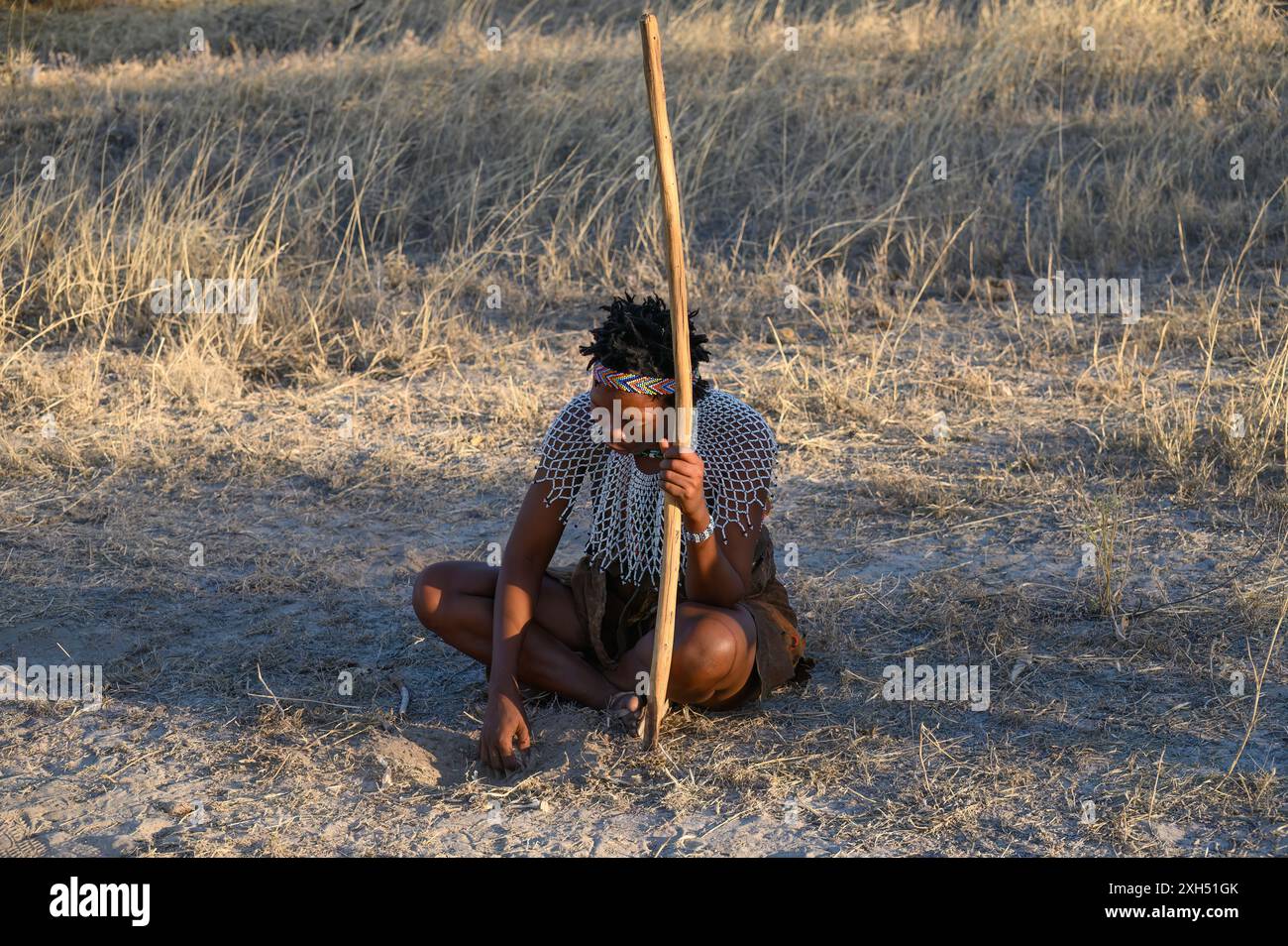 A female San bushmen, adorned with beadwork, sitting cross legged on ...