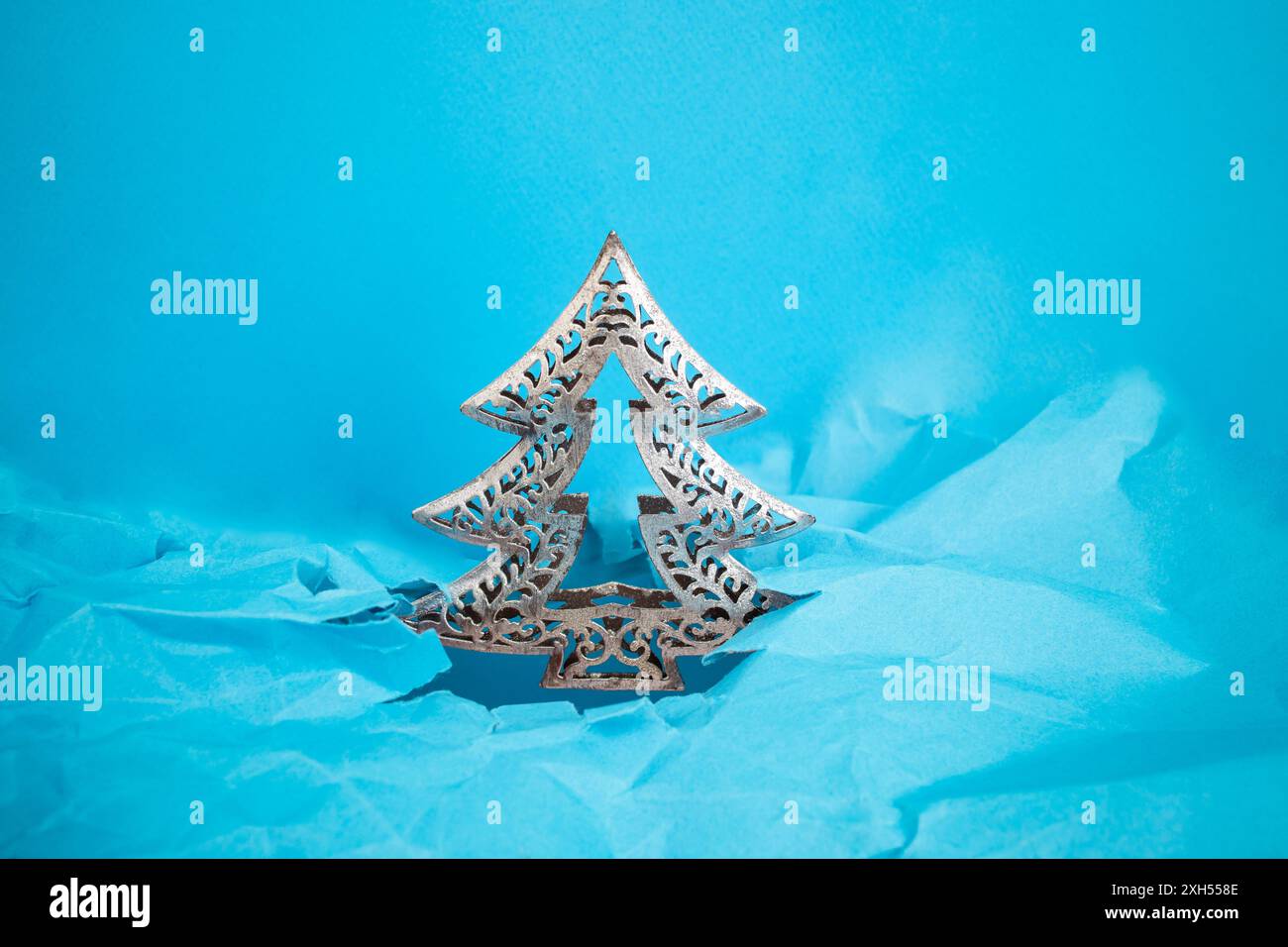 Silver metallic fir tree structure emerging thru ripped paper hole ...