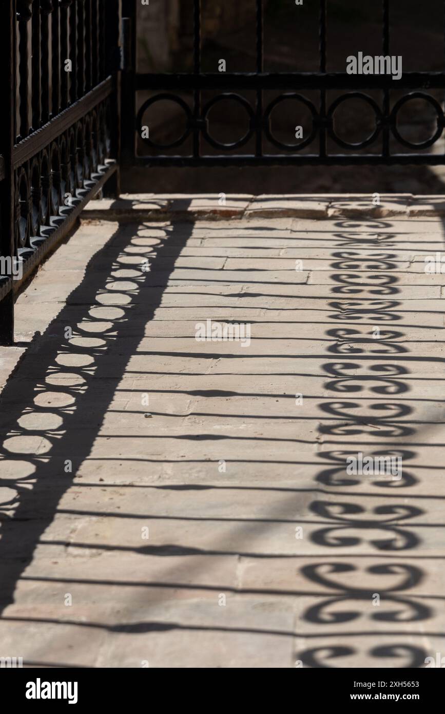Shadows from an ornate railing cast onto a stone floor, creating ...