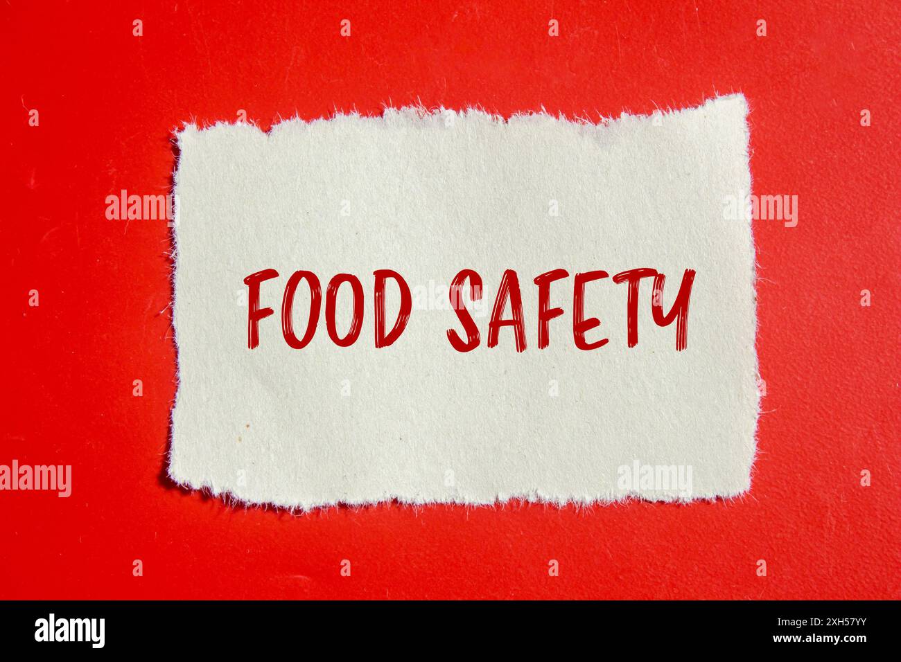 Food safety message written on ripped torn paper piece with red background. Conceptual food ...