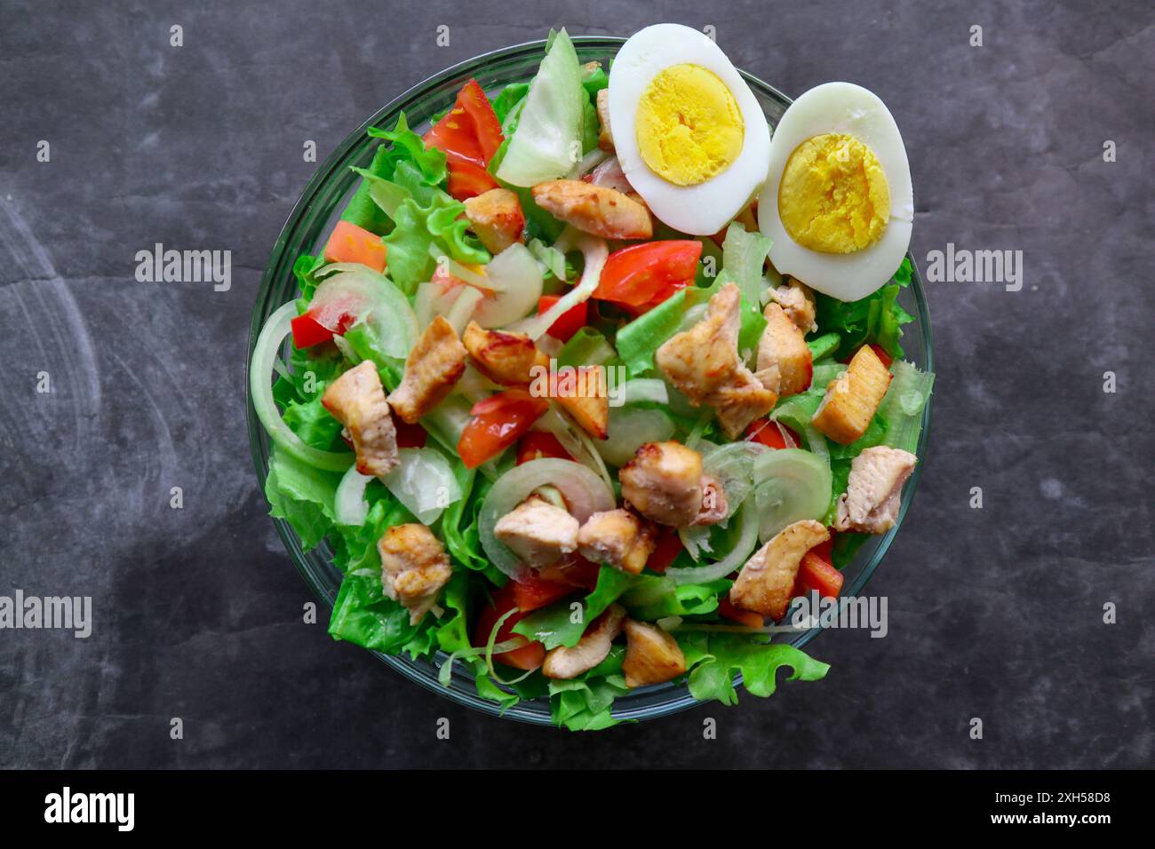 A cesar salad bowl filled with lettuce, tomatoes, egg and chicken. The ...