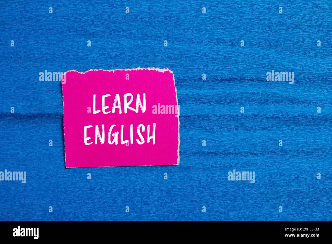 Learn english message written on ripped torn pink paper piece with blue background. Conceptual ...