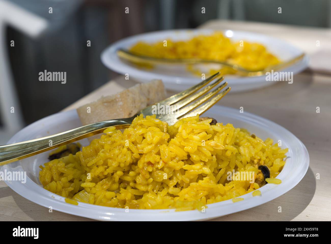 Two plates of spanish paella with a fork on it and a slice of bread ...