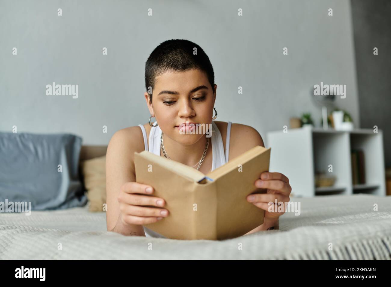 A young woman with short hair in casual wear reclining on a bed ...