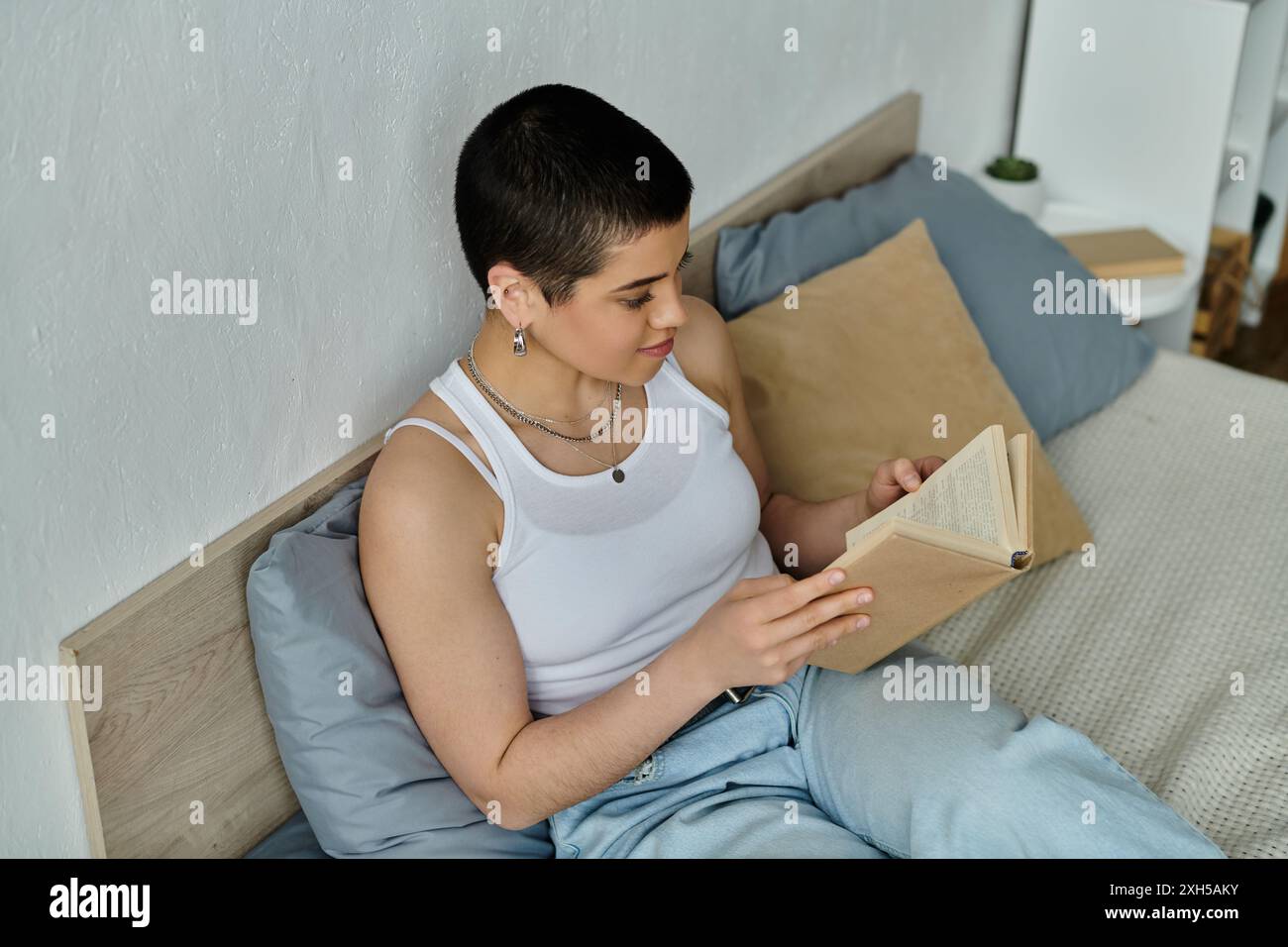 A young woman with short hair in casual wear sitting on a bed, deeply ...