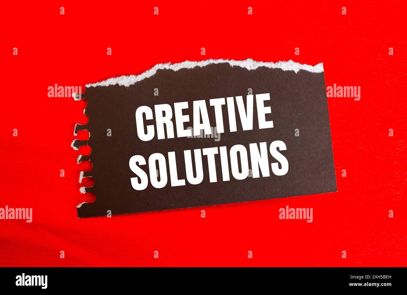 Creative solutions message written on ripped torn black paper piece with red background ...