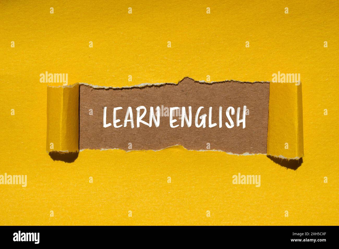 Learn english message written on ripped torn yellow paper with brown background. Conceptual ...