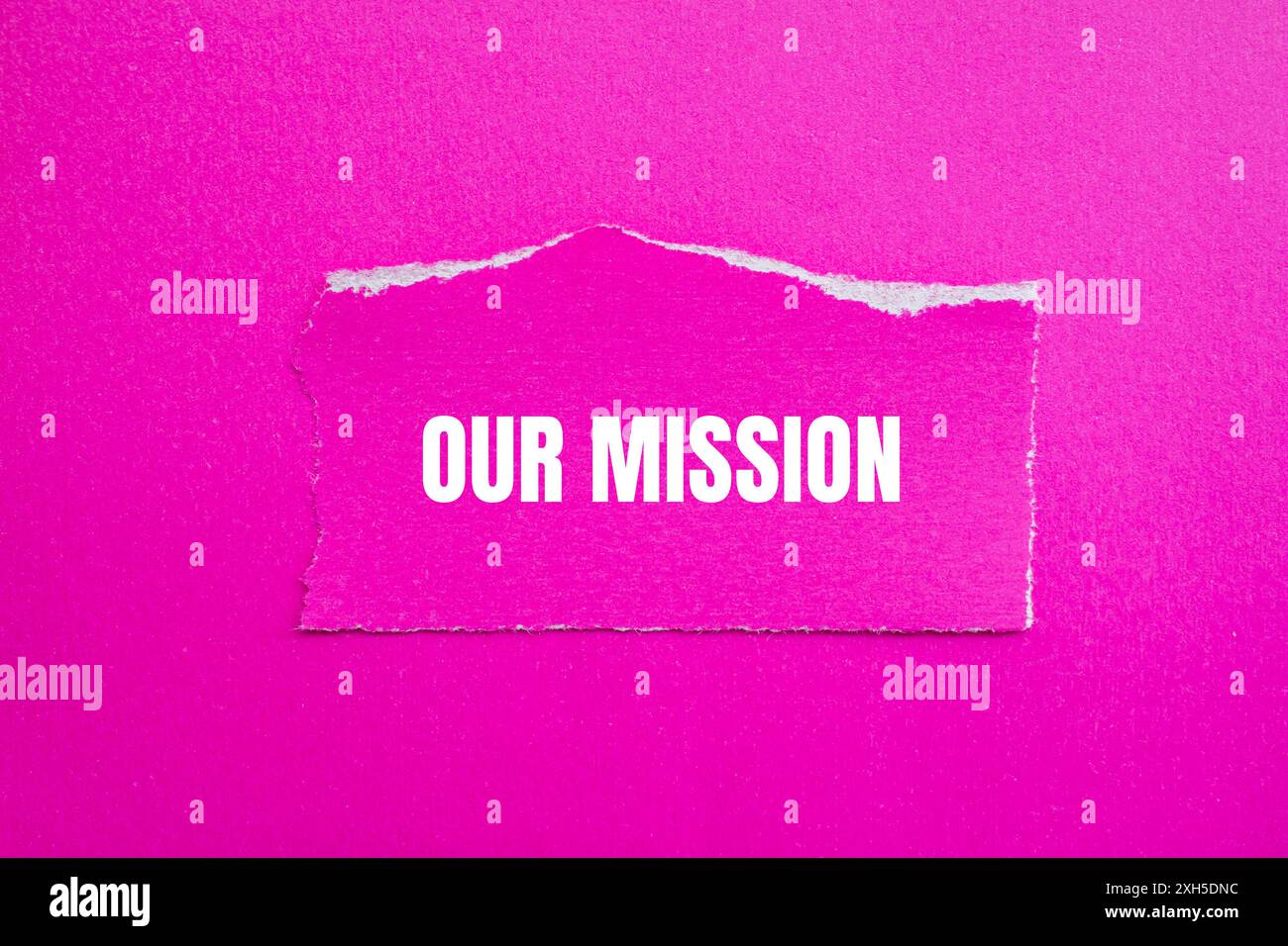 Our mission message written on ripped torn pink paper piece with pink background. Conceptual our ...