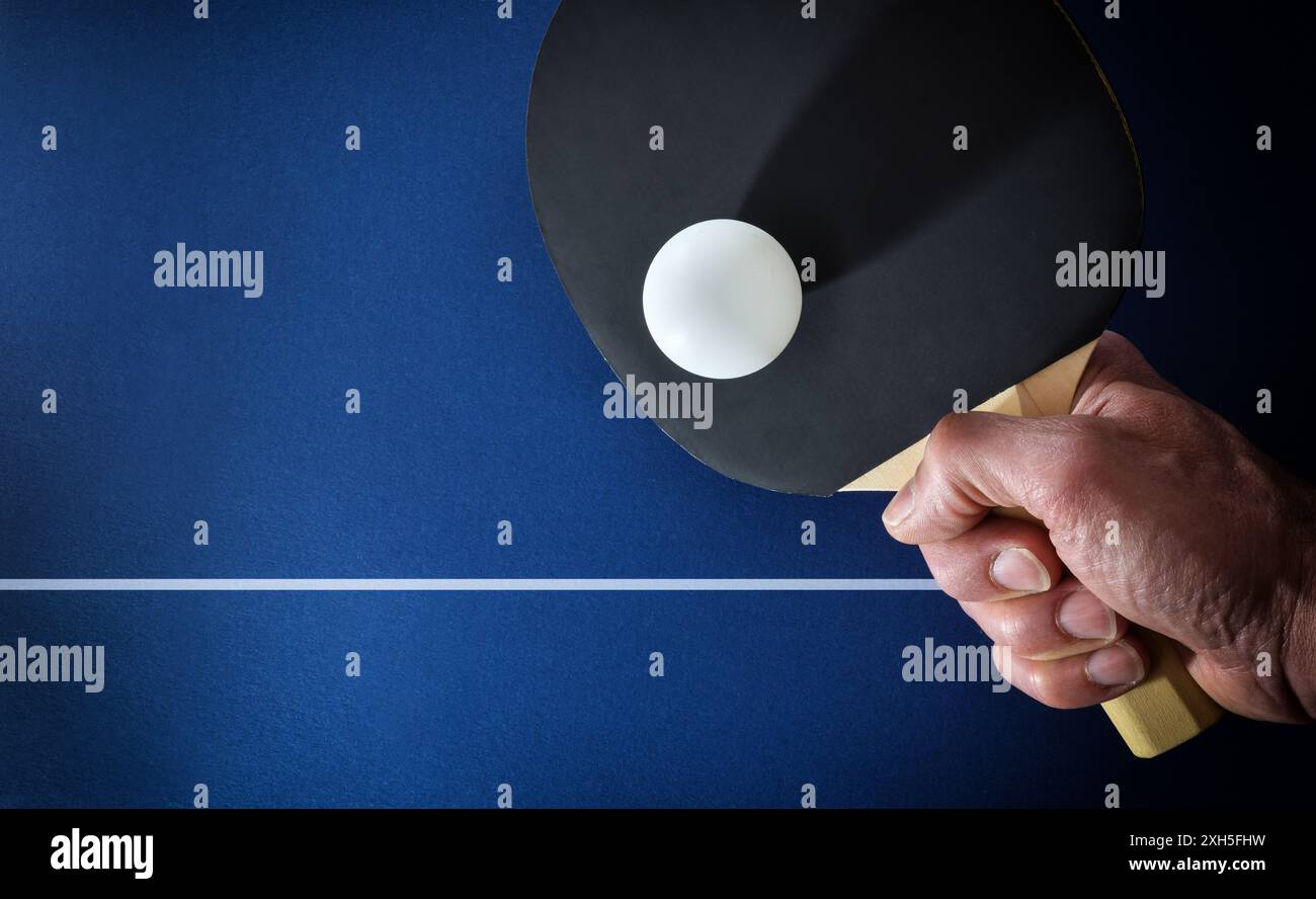 Detail of hand with table tennis paddle hitting a white ball on a blue ...