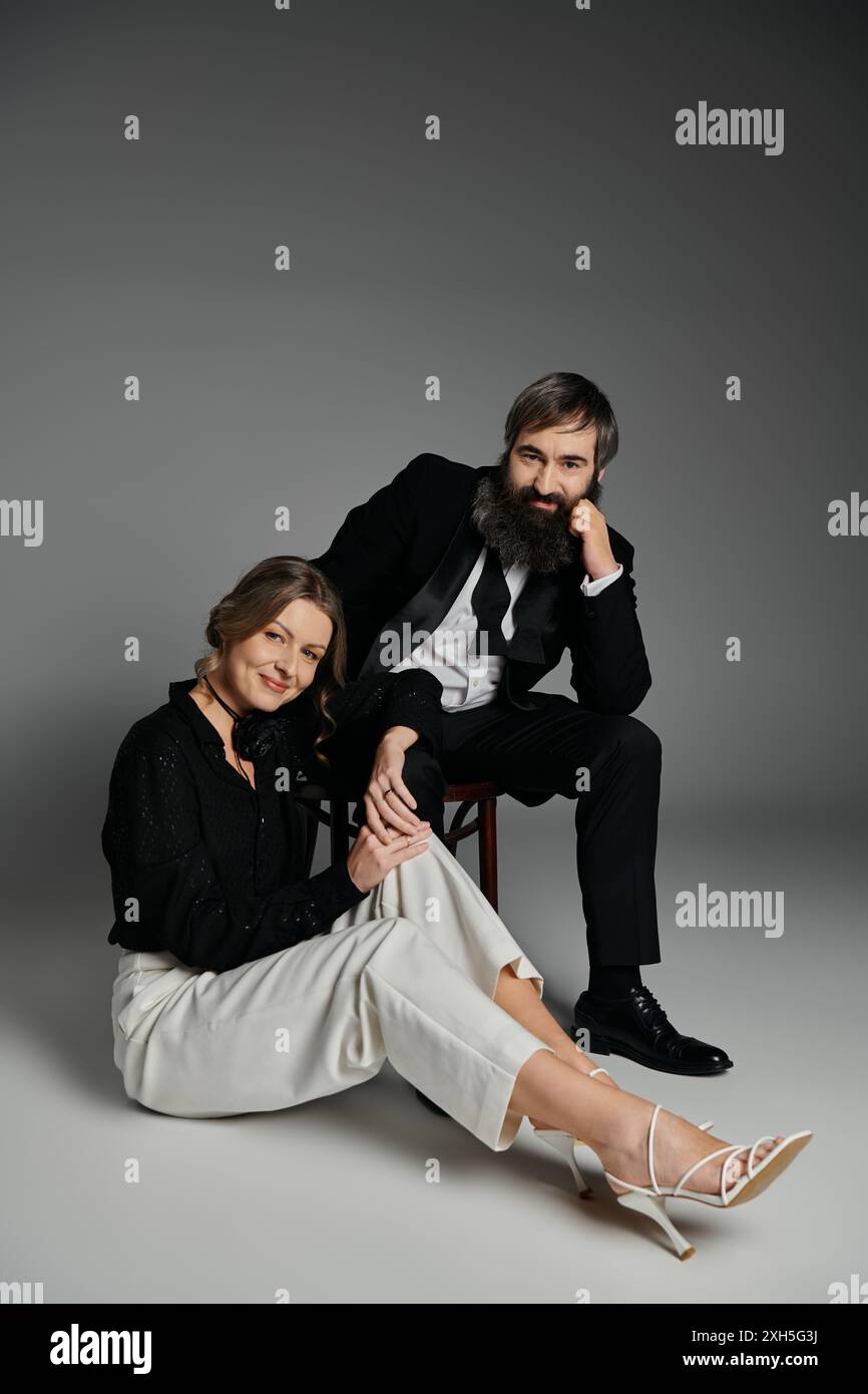 A loving couple dressed in formal attire pose together against a gray ...