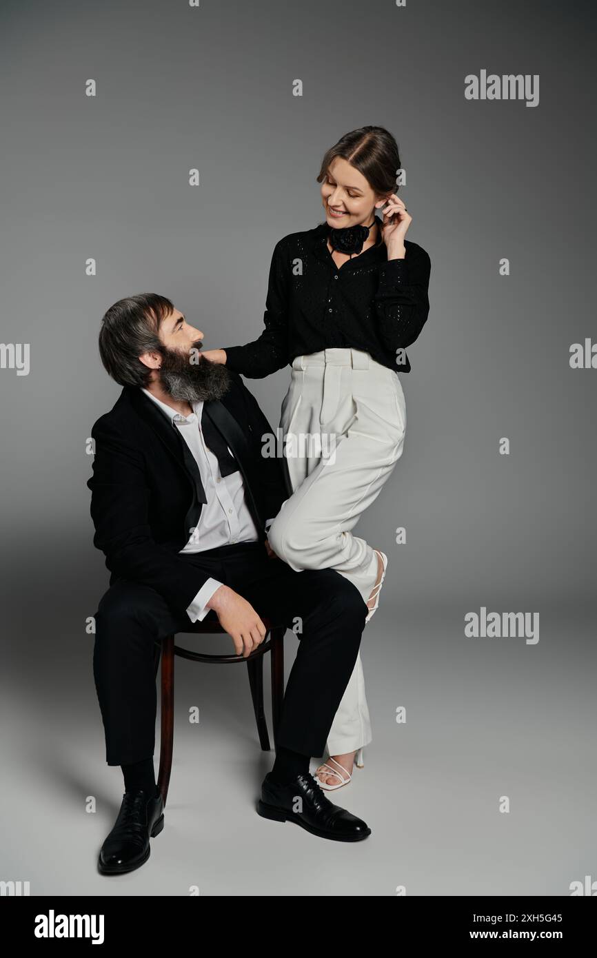 A couple in elegant clothing pose together, the woman standing on a ...