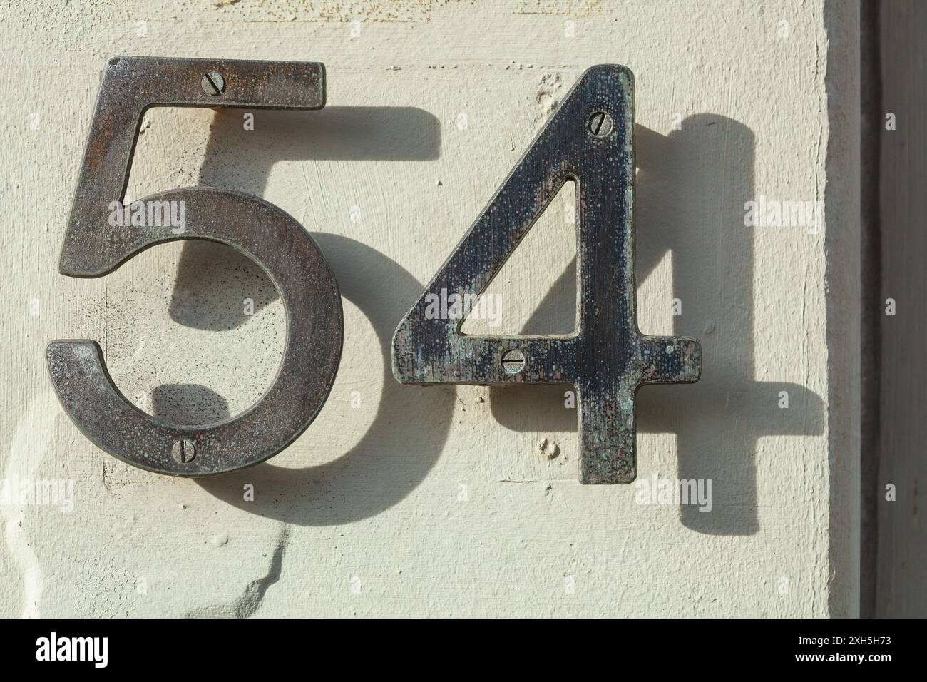 Black metal house number sign number fifty-four with shadow on a white ...