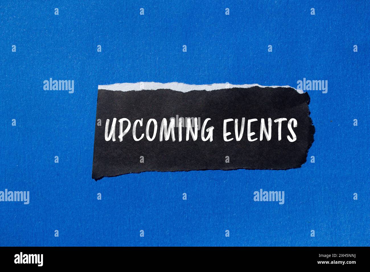 Upcoming events message written on ripped torn black paper piece with blue background ...