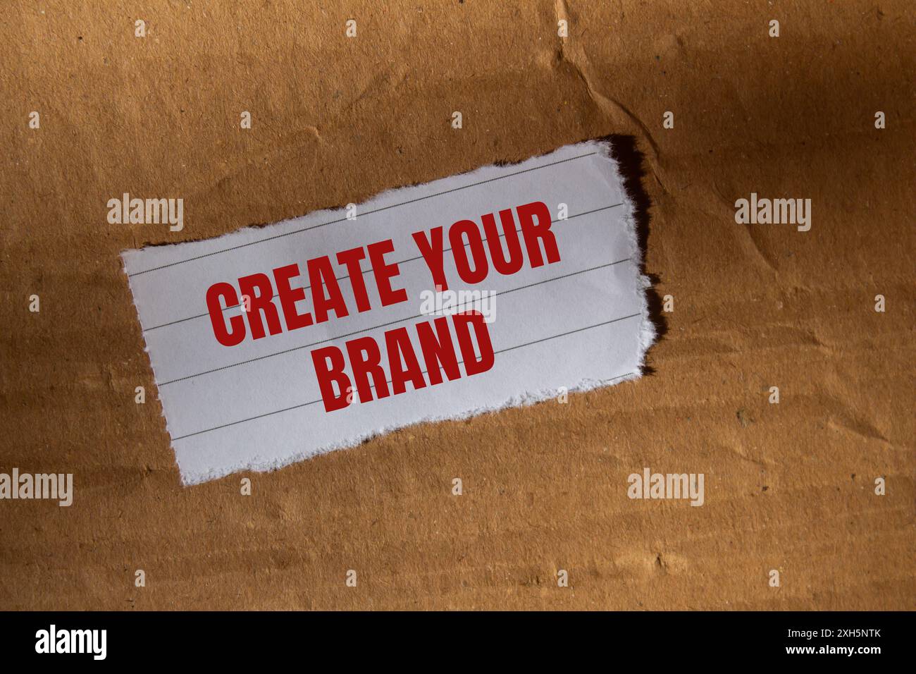 Create your brand message written on ripped torn white paper piece with cardboard background ...