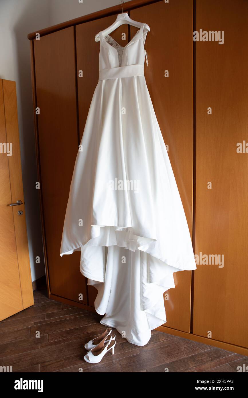 Elegant white wedding dress hanging on a hanger in front of a wooden ...