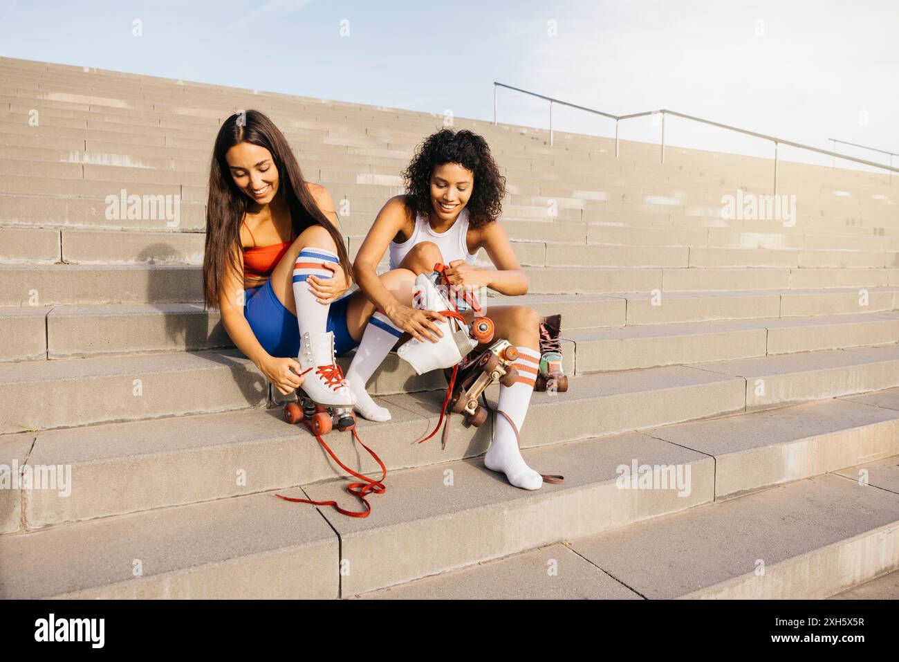 Two friends sitting on steps, putting on their roller skates and ...
