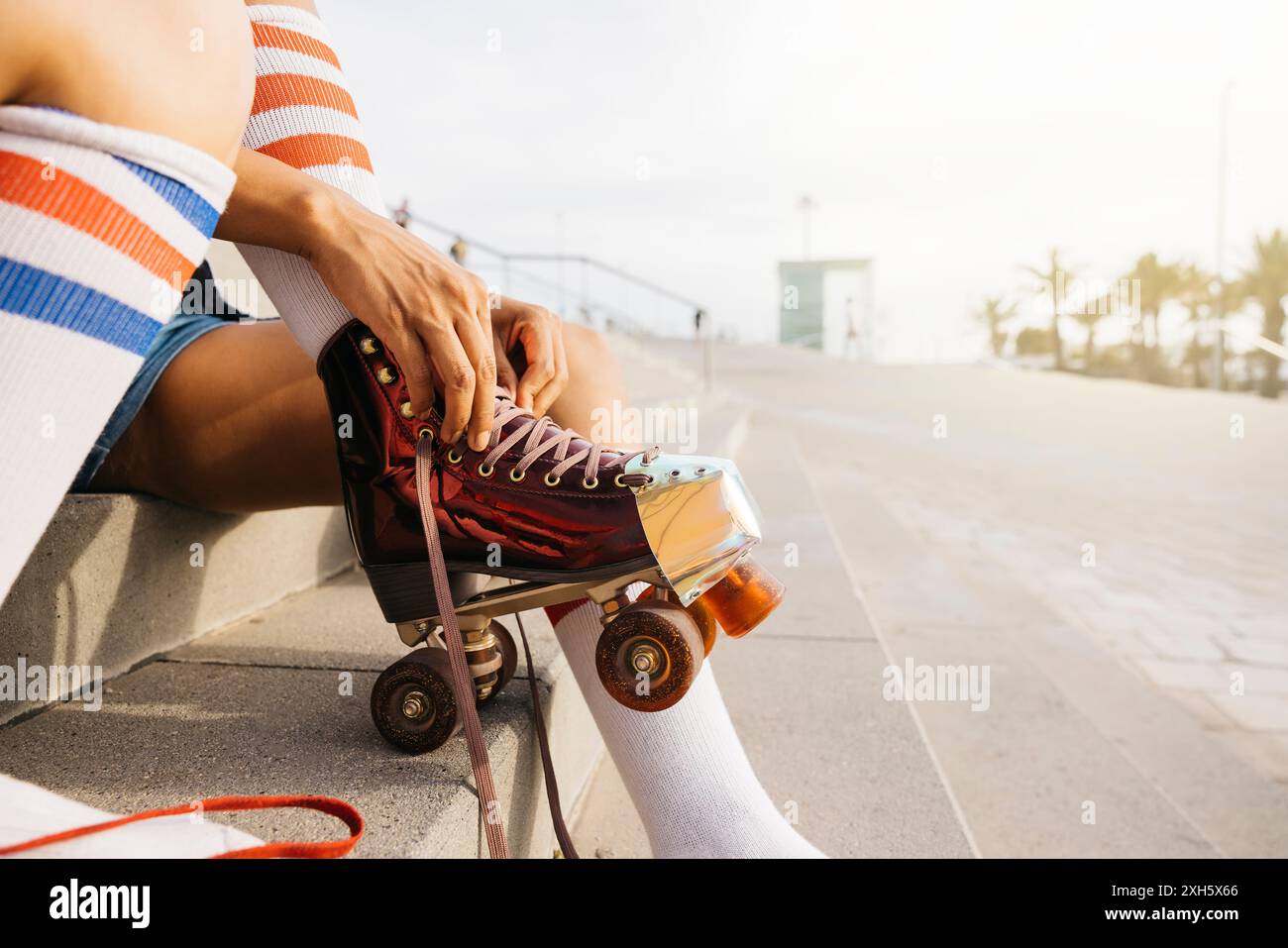 Close up of a young woman lacing up a pair, sitting on steps, of roller ...