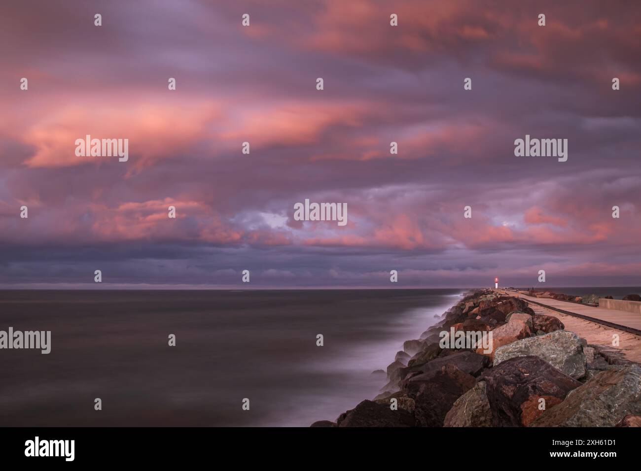 Sunset with pink stormy sky over rocks and lighthouse, The Spit Stock ...