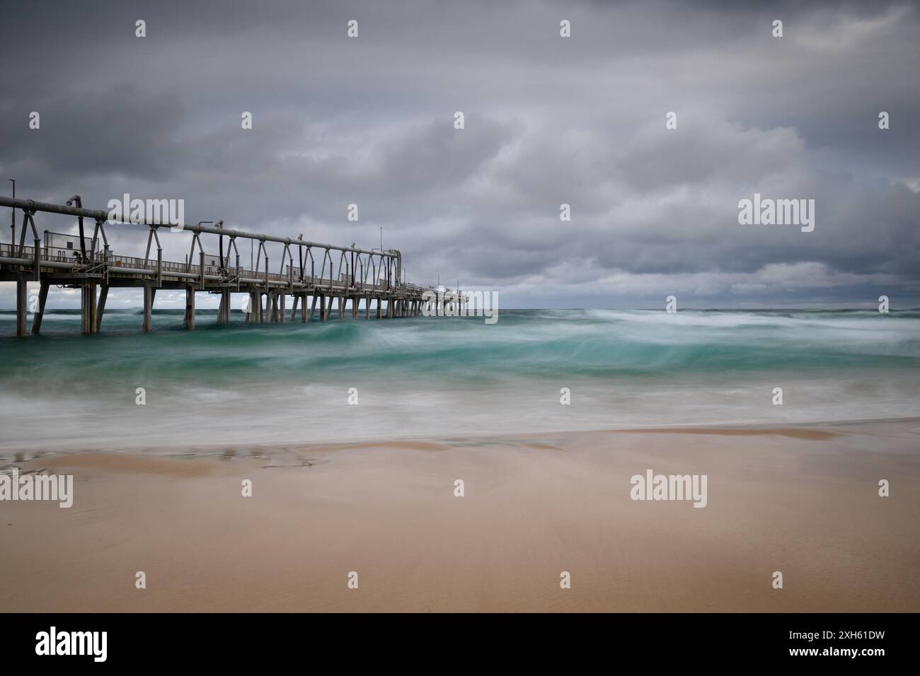Moody story beach with pier and waves under a cloudy sky, The Spit ...