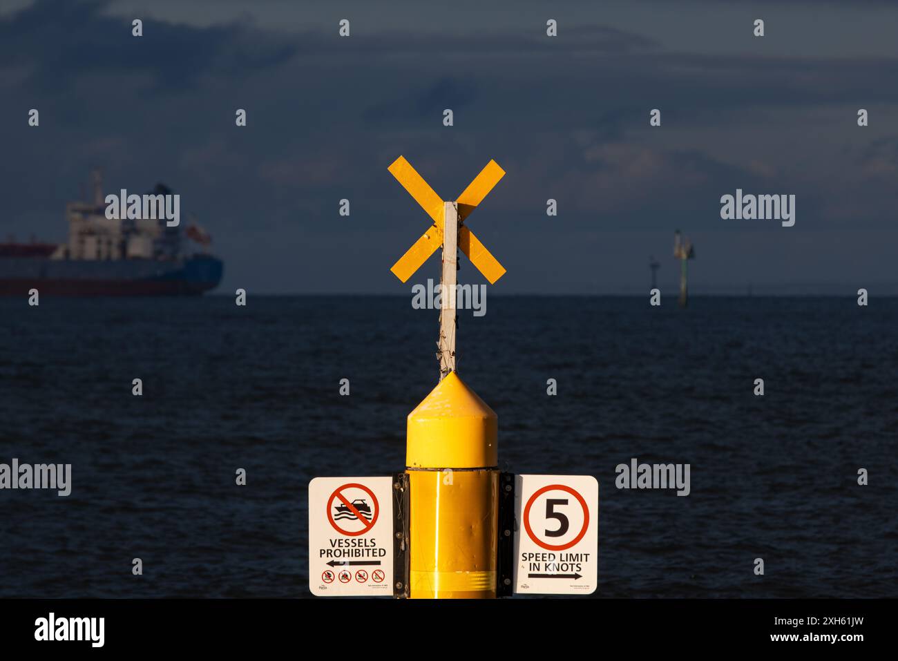 Yellow marine navigation marker with signs and ship in the background ...