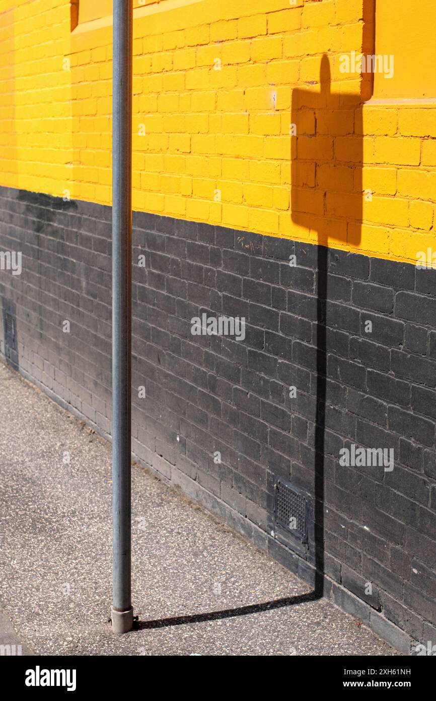 Urban street pole casting a shadow on a yellow and black wall Stock ...