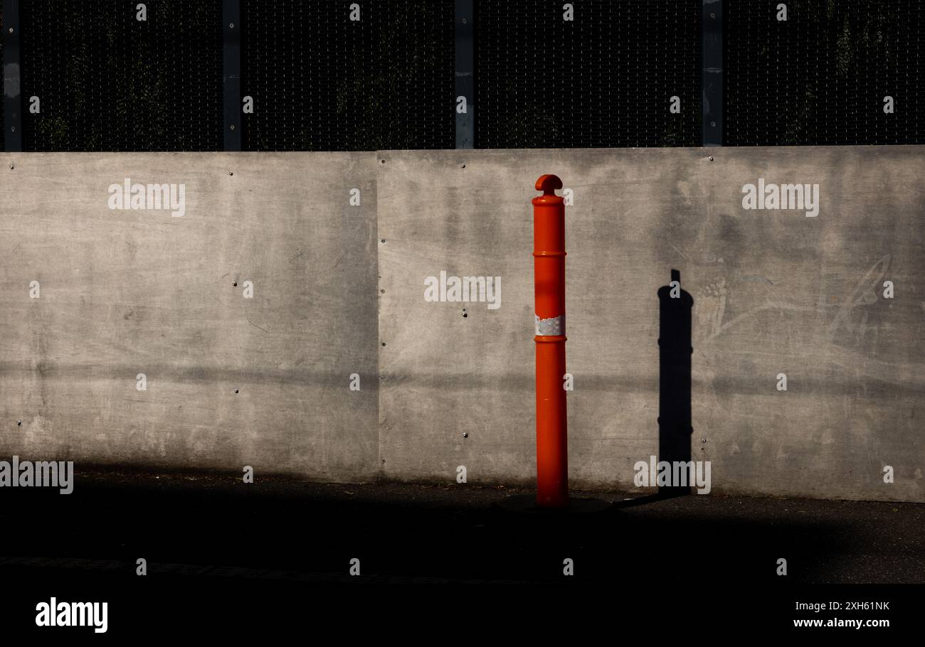 Red safety bollard casting a long shadow against a concrete wall Stock ...