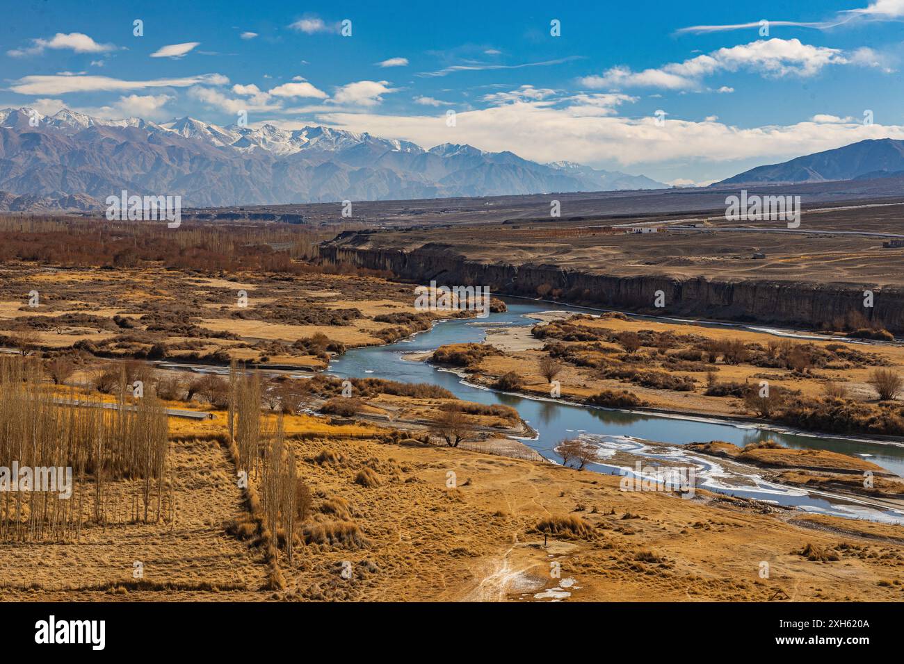 Indus river flowing through dry winter grass with snow-clad mountains ...