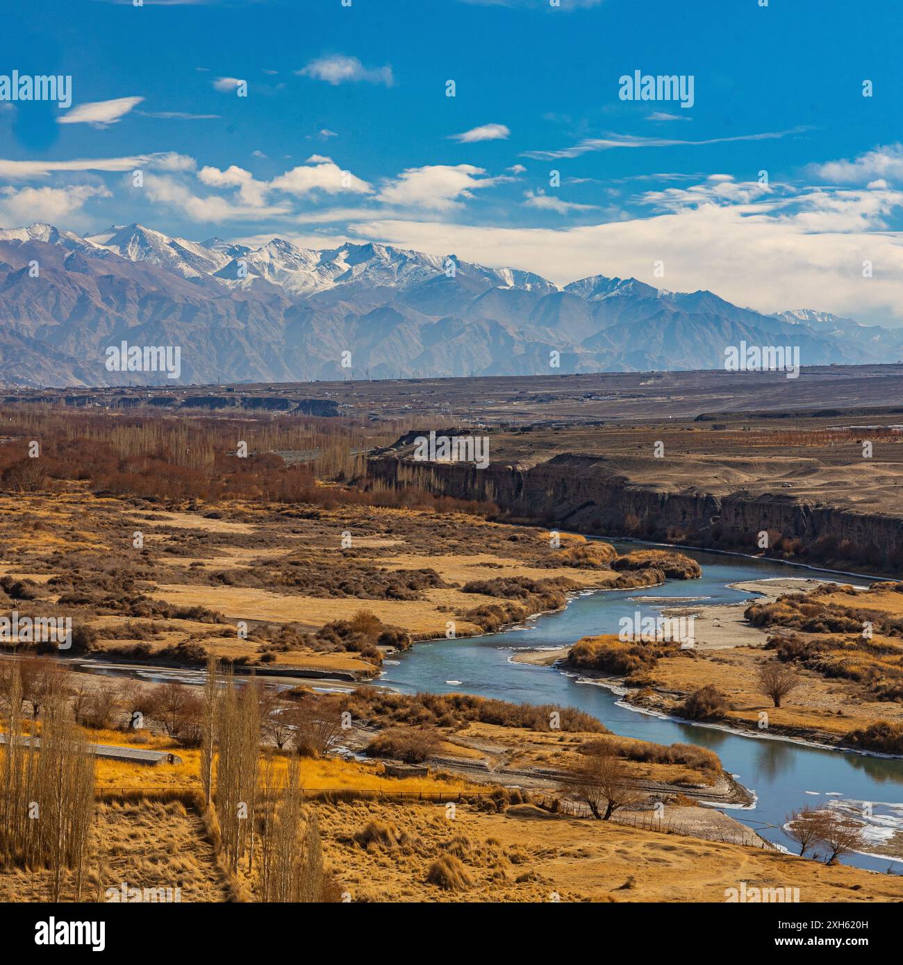 Indus river flowing through dry winter grass with snow-clad mountains ...