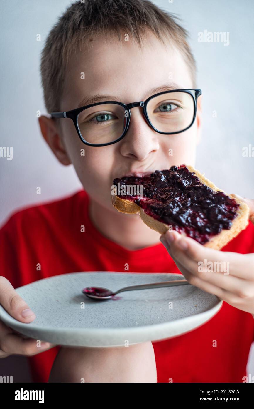 Nice boy in red t-shirt eating toast Stock Photo - Alamy