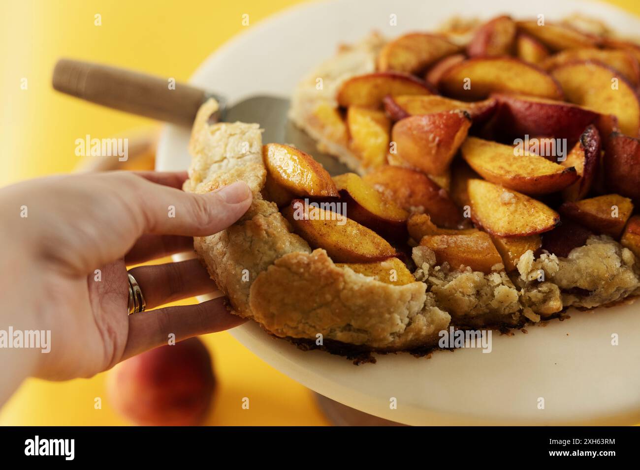 Hand serving a slice of peach galette on a yellow background Stock ...